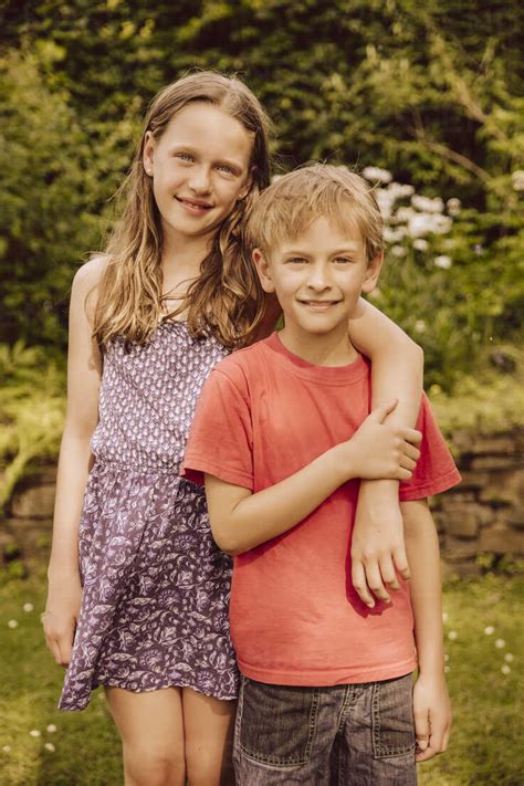 Smiling Girl Putting Arm Around Brother In Garden Stock Photo