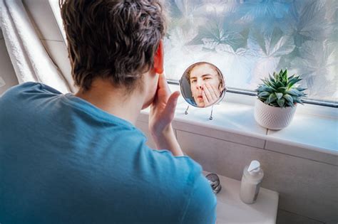 여드름 문제가있는 집중된 백인 십대 소년은 집에서 얼굴 피부를 돌 봅니다 그는 거울을보고 욕실에서 세안 로션으로 얼굴을 청소합니다 십대 피부 관리 과정 16 17 살에 대한