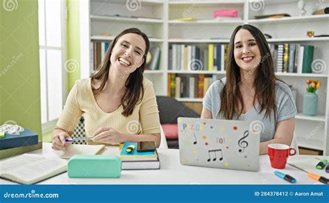 Two Women Sitting On Table Studying Using Laptop Writing Notes At Library University Stock Photo