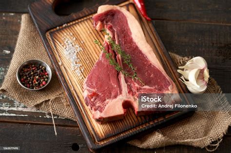 나무 도마에 수분이 많은 신선한 노련한 T 뼈 스테이크 위에 로즈마리의 잔가지와 함께 삼베의 조각에 후추 붉은 칠리의 포드 마늘의 머리 비스듬히 정상 보기 텍스트장소 0명에