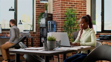 African American Woman Analyzing Charts On Papers And Laptop Stock