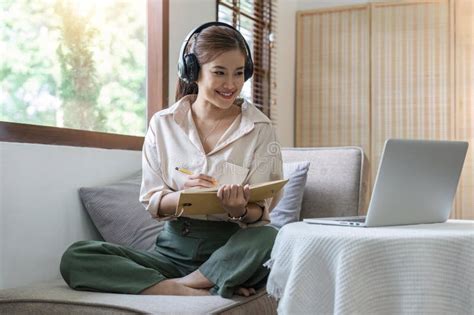 woman taking notes in notebook while using laptop at home in living