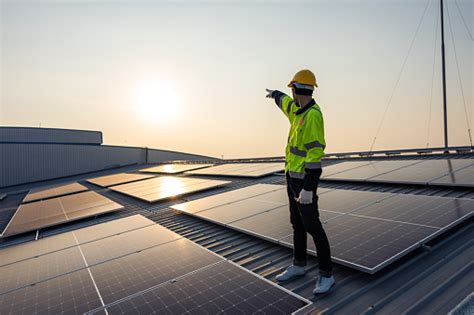 전문 엔지니어가 태양광 패널 시스템의 유지 보수를 위해 일합니다 지붕에서 일하는 매력적인 기술자는 일몰 동안 태양 전지 분야에서 태양 전지 패널 장비 상자를 검사하고