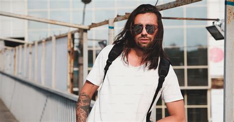 거리에서 긴 머리 라이프 스타일을 가진 세련된 힙 스터 모델 도시에서 흰색 티셔츠와 찢어진 청바지를 입고 사진