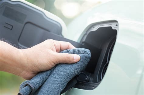 자동차 소유자의 손은 전기 자동차 충전 커넥터를 천으로 조심스럽게 청소하여 사용 전후에 먼지와 습기가 없는지 확인합니다 안정적인 충전을 위한 유지보수의 중요성 검사 보기에