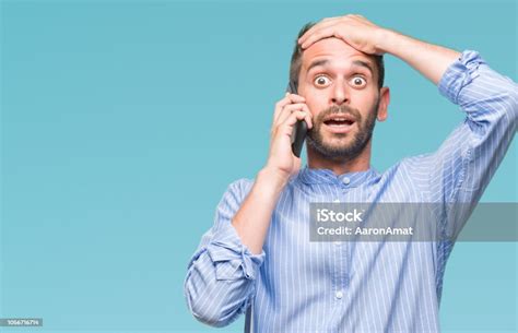 젊은 잘생긴 사람은 전화에 손으로 머리에 압박 절연된 배경 위에 충격 수치심과 깜짝 얼굴로 분노와 좌절 두려워 하 고 실수에 대 한 화가 전화 사용에 대한 스톡 사진 및