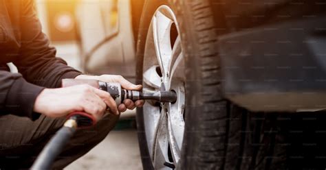 전기 드라이버를 가진 자동차 정비사가 밖에서 타이어를 교체합니다 자동차 서비스 손은 바퀴의 타이어를 교체합니다 타이어 설치 개념입니다 사진 Unsplash의 바퀴 이미지