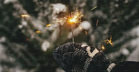 눈 속의 소나무 가지를 배경으로 불타는 폭죽을 들고 아늑한 장갑을 낀다 새해 복 많이 받으세요 분위기 있는 마법의 순간 저녁에 빛나는 불꽃놀이를 하는 여자 손 즐거운