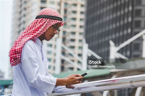 스마트 폰 응용 프로그램을 사용하는 이슬람 남자는 스마트 폰 무슬림 현대 아랍 도시를 들고 손에 일정 의제를 구성합니다 아랍 남성 착용 히잡과 무슬림 정장 드레스 보내는