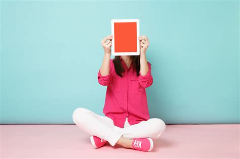 장미 셔츠 블라우스에 전체 길이 세로 여자 바닥에 앉아 흰 바지 잡고 밝은 핑크 블루 파스텔 벽 배경 스튜디오에 고립 된 태블릿 Pc 패션 라이프 스타일 개념입니다 복사