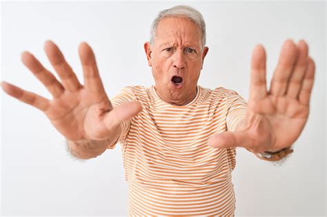 고립 된 흰색 배경 위에 서있는 줄무늬 티셔츠를 입은 선임 회색 머리의 남자가 손바닥 화가 나고 좌절하는 표정으로 중지 제스처를