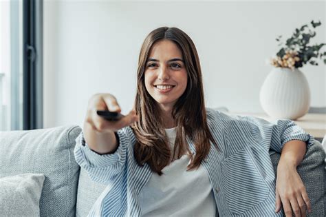 전원을 켭니다 행복한 밀레니엄 세대 여성 사용자는 거실의 소파에 앉아 스마트 Tv 세트 에어컨 홈 시어터 시스템을 제어합니다 젊은 여성 고객 손에 적외선 원격 제어 장치에