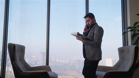 창문 옆에 서서 현대 사무실에서 서류와 문서를 확인하면서 전화 통화를 하는 젊은 사업가 25 29세에 대한 스톡 사진 및 기타