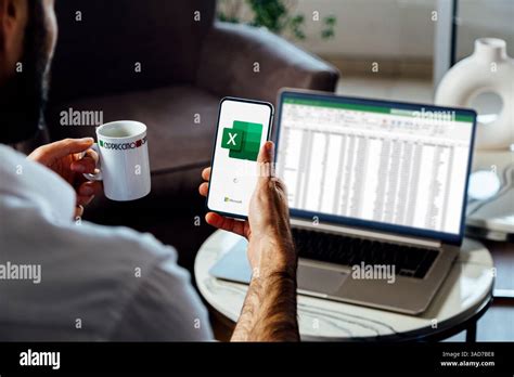 Man Using A Mobile Phone Displaying Logo Of Microsoft Excel On The