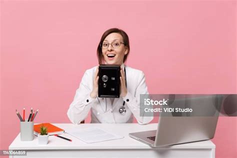 여성 의사는 의료 문서 보류 은행 파스텔 핑크 배경에 고립 된 병원에서 컴퓨터에 책상 작업에 앉아 의료 가운 안경 청진에 여자 헬스케어 의학 개념 건강관리와 의술에 대한