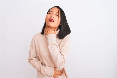 고립된 흰색 배경 위에 서있는 터틀넥 스웨터를 입은 젊은 중국 여성은 고통스러운 목 독감 클로드 및 감염에 대한 목의 통증에