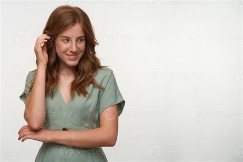 Indoor Shot Of Beautiful Redhead Female With Shy Smile Looking Aside And Touching Her Hair