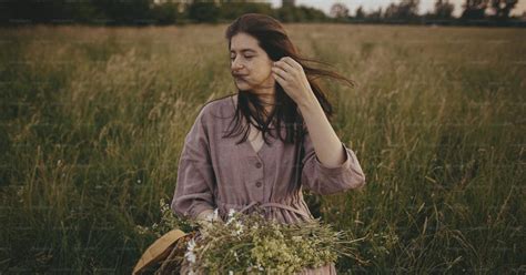 바람이 부는 머리와 린넨 드레스를 입은 아름다운 여자가 여름 초원에서 꽃다발과 함께 나무 의자에 앉아 있다 저녁 시골에서