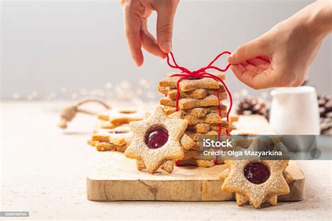 쿠키 선물을 준비합니다 여자는 빨간 면 보우 코드를 묶는 손 빨간 리본으로 묶인 라즈베리 잼을 곁들인 수제 별 또는 꽃 모양의 린저 쿠키 크리스마스 또는 어머니의 날 선물