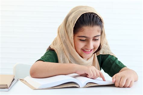 아름다운 눈을 가진 행복한 무슬림 학생 소녀는 히잡 전통 의상을 입고 테이블에서 공부하고 숙제를 하고 아이는 하얀 배경에 책을 읽고 아동 여성 교육을 하고 양성 평등을