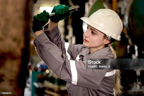 보호용 작업복을 입고 안전하게 헬멧을 쓴 산업 엔지니어 여성은 제조 공장에서 렌치를 사용하여 기계를 수리합니다 제강 금속 산업에서 기계를 수리하는 아름다운 여성 노동자 30