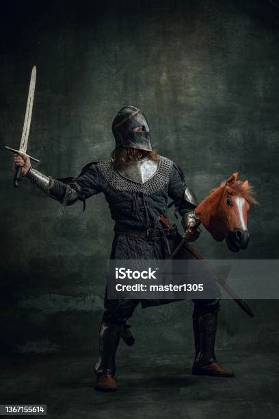 헬멧과 갑옷을 타고 장난감 말을 입고 어두운 배경에 고립 된 큰 칼을 들고 중세 전사 또는 기사의 초상화 시대 역사의 비교 기사 사람의 역할에 대한 스톡 사진 및 기타