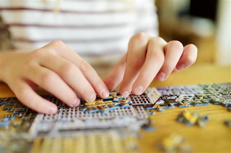 집에서 퍼즐을 맞추는 아이의 손에 클로즈업 거실 테이블에 직소 퍼즐 조각을 연결하는 아이 직소 퍼즐을 조립하는 아이 아이들을위한