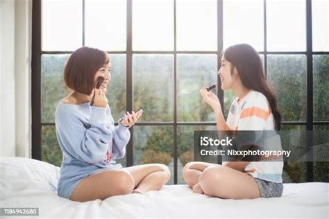 Two Asian Girls Having Fun While Applying Make Up On The Bed Stock