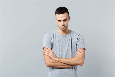 캐주얼 옷 카메라를 찾고에 화가 엄격한 젊은 남자의 초상화 손을 잡고 스튜디오에서 회색 벽 배경에 고립 된 교차 사람들은 진심으로 감정 라이프 스타일 개념입니다 복사 공간을