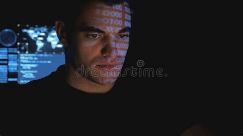 Man Programmer Hacker Working on a Computer while Blue Code Characters Reflect on His Face in a ...