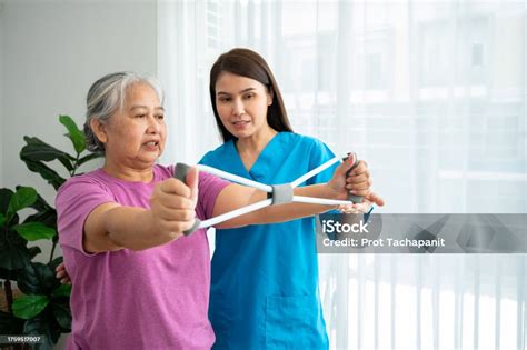 물리 치료 센터에서 팔 근육 회복을 위한 젊은 물리치료사와 함께 고무 확장기로 운동하는 행복한 노인 여성 간병인과 건강의 보살핌으로 행복한 은퇴의 개념 2명에 대한 스톡