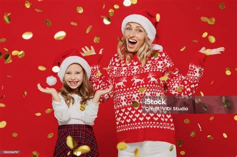 스웨터 모자를 쓴 젊은 즐거운 여자는 67 세의 어린 소녀와 재미를 느낍니다 엄마 어린 아이 딸은 일반 빨간색 색상 배경 스튜디오에서 고립 된 색종이를 던지며 새해 사랑