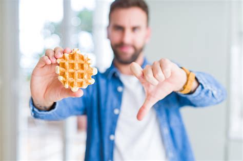 화난 얼굴로 달콤한 벨기에 팬케이크를 먹는 잘생긴 남자 부정적인 기호는 아래로 엄지 손가락으로 혐오를 보여주는 거부 개념 가정 생활에 대한 스톡 사진 및 기타 이미지