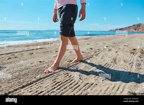 A Person Walking Barefoot Along A Textured Sandy Beach With Clear Skies