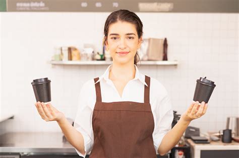 아름다운 백인 바리스타 여성이 팔을 펼치고 커피 바에서 두 손에 테이크 아웃 커피 컵을 보여줍니다 25 29세에 대한 스톡 사진 및 기타 이미지 Istock
