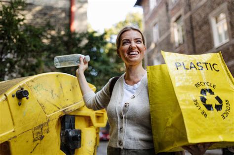 Woman Throwing Plastic Waste Bottles Into Recycling Container In Front