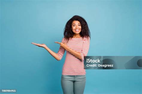 사진 의 쾌활한 흥분 미친 쾌활한 좋은 귀여운 달콤한 달콤한 예쁜 검은 여자 친구는 파란색 선명한 색상 배경 위에 고립 된 회색 바지 바지를 입고 그녀의 손바닥에 빈 공간을