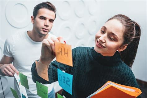 두 젊은 비즈니스 동료 스마트 사무실에서 유리 벽에 스티커 노트에 게시 된 프로젝트 계획 동안 회의 있다 그룹 프로젝트에 대 한