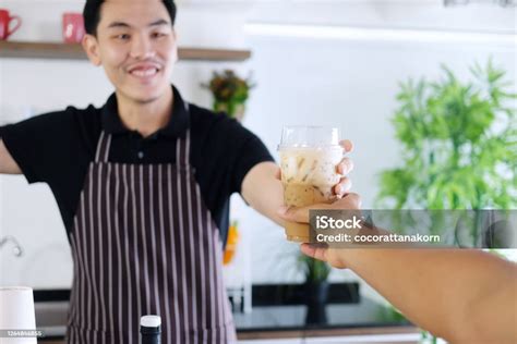커피숍카운터바에서 아이스 라떼 커피 한 잔을 마시며 미소짓는 아시아 바리스타 청년 투명 플라스틱 유리를 들고 손에 초점을 닫습니다 2명에 대한 스톡 사진 및 기타 이미지