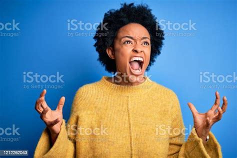 젊은 아름 다운 아프리카 계 미국인 Afro 여자 곱슬 머리 를 입고 노란 캐주얼 스웨터 미친 미친 소리와 공격적인 표정과 팔을 제기 고함 좌절 개념입니다 감정에 대한 스톡