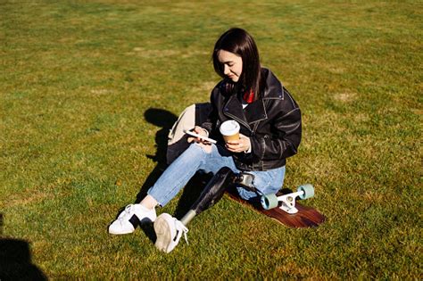 의족을 착용한 젊은 여학생이 대학 캠퍼스의 푸른 잔디밭에 앉아 있다 생체 공학적 다리를 가진 장애인 여성 전화기를 사용하는 다리 보철 장비를 착용한 여성 의지에 대한 스톡