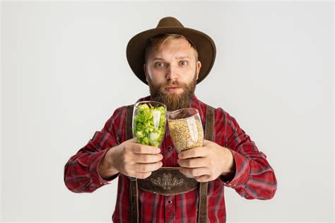 모자를 쓴 젊은 수염을 기른 남자와 전통적인 바이에른 의상을 입고 야생의 뜨겁고 보리가 가득한 맥주 잔을 들고 있습니다 축하 옥토버 페스트 축제 개념 10월에 대한 스톡