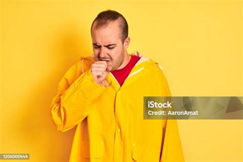 고립 된 노란색 배경 위에 서있는 비옷을 입은 젊은 남자는 감기 또는 기관지염의 증상으로 기분이 좋지 않고 기침합니다 헬스케어 개념 가을에 대한 스톡 사진 및 기타 이미지