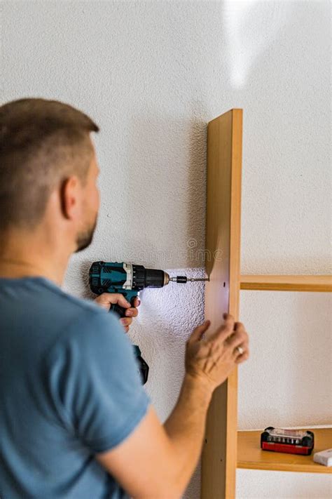 Young Man Assembling Wooden Shelf With Electric Drill While Diy And