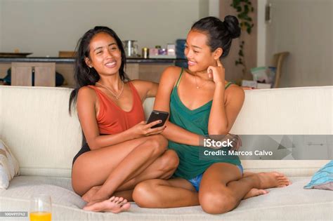 아름 다운 영과 행복 한 아시아 여자 친구 또는 자매 인터넷 소셜 미디어 모바일 함께 재미를 즐기는 쾌활 하 고 여자 들 우정에 웃음을 웃 고 소파 소파 집에서 전화 2명에