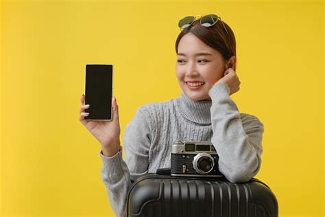 여성 아시아 관광객의 초상화 카메라와 수하물 회색 셔츠 노란색 배경에 고립 된 모바일 응용 프로그램을 제시하기위한 빈 템플릿