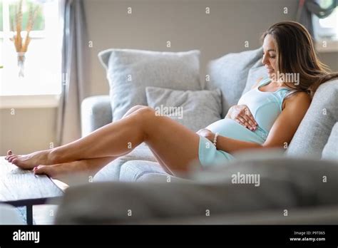 Smiling pregnant woman in dress lying on the sofa touching her belly Stock Photo - Alamy