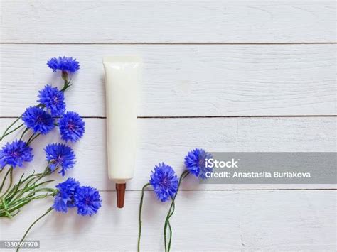 긴 노즐과 청동 나사 캡과 나무 흰색 테이블에 파란색 야생 꽃과 아이보리 스퀴즈 화장품 튜브의 모형 브랜딩용 병 상단 보기 플랫
