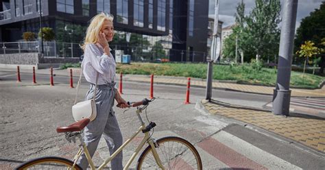 비즈니스 파트너와 휴대폰으로 통화하는 동안 손에 자전거를 들고 횡단보도를 걷고 있는 세련된 여성 사진 Unsplash의 유행 이미지