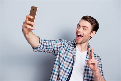 수염 매력 긍정적인 Brunet 남자 캐주얼 복장에서 주말 여행 Selfie 회색 배경 위에 평화 기호 전면 카메라를 몸짓을 촬영 하는 데 휴일 셔츠 체크 무늬 가정용